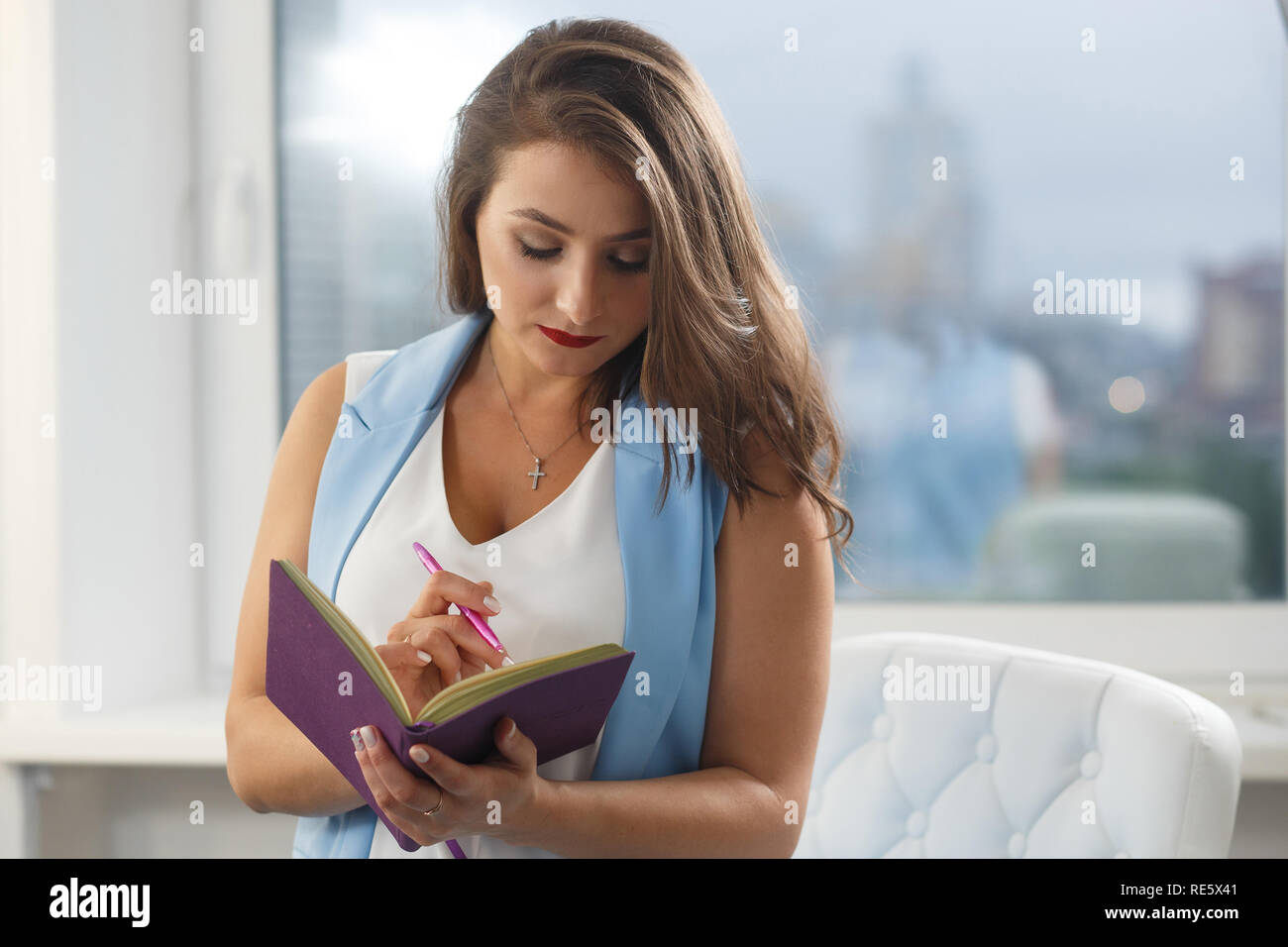 Beautiful woman with perfect makeup writing notes in purple notebook ...