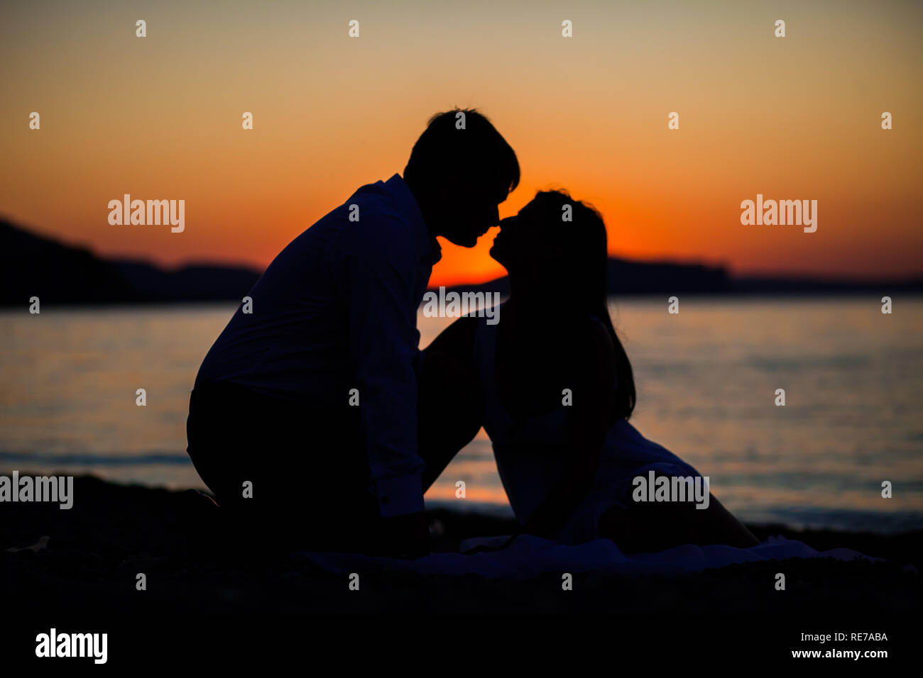 Couple sitting on sunset background Stock Photo - Alamy