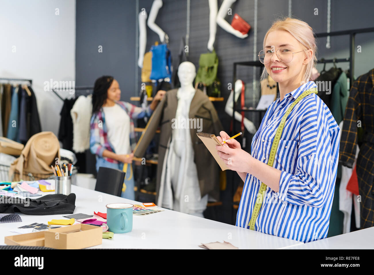 Portrait of young smiling tailor standing and drawing sketches while ...