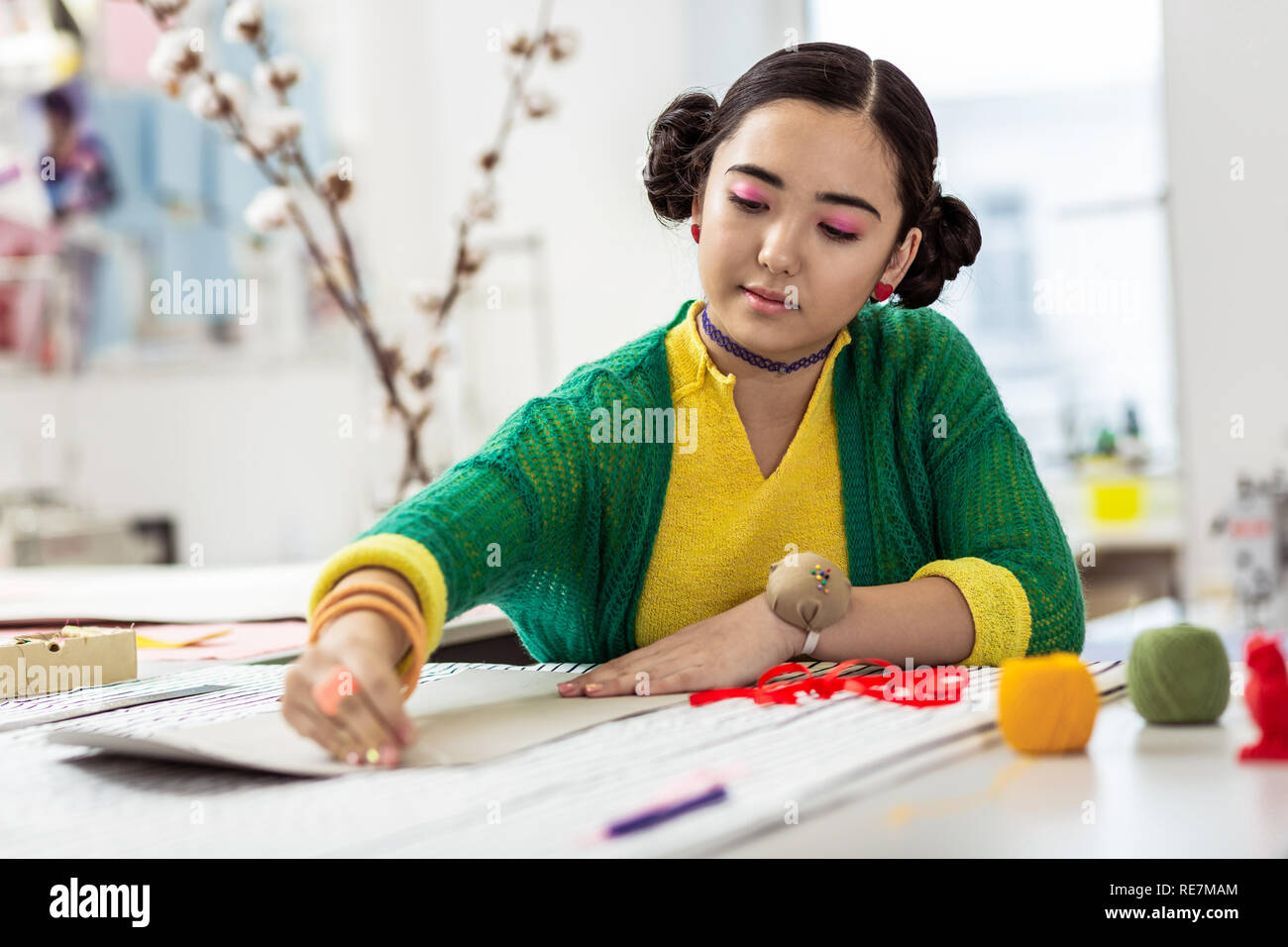 Cute brunette asian dressmaker with pink eyeshadows looking focused ...