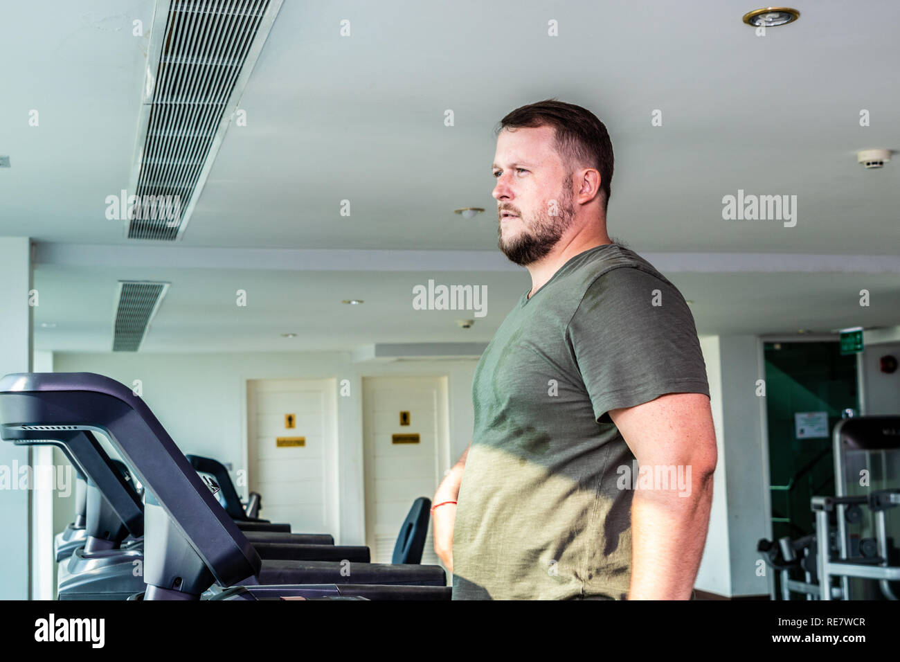 Sweating chubby man walking on running track, warming up on gym ...