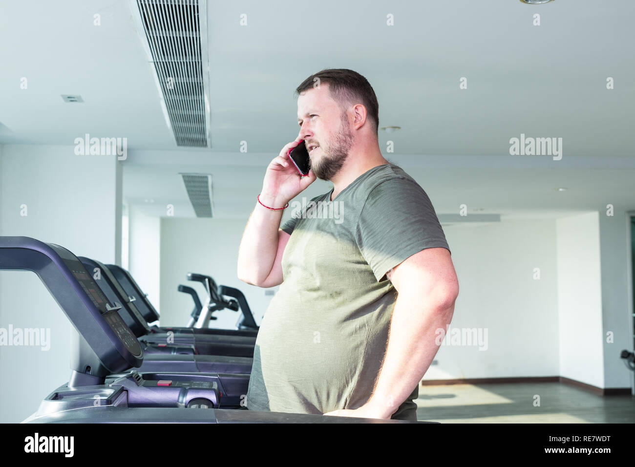 Sweating chubby man walking on running track, warming up on gym ...