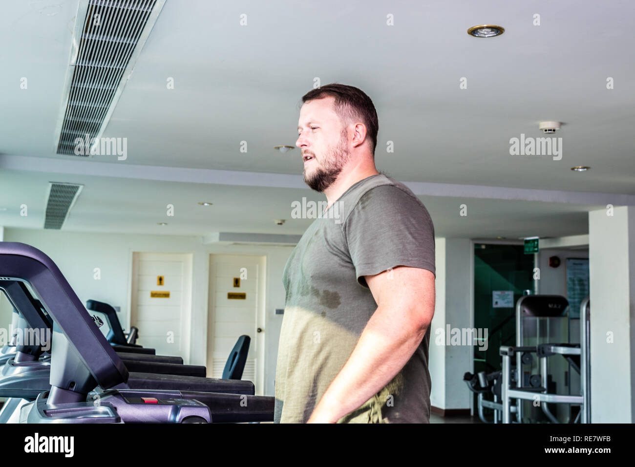 Sweating chubby man walking on running track, warming up on gym ...