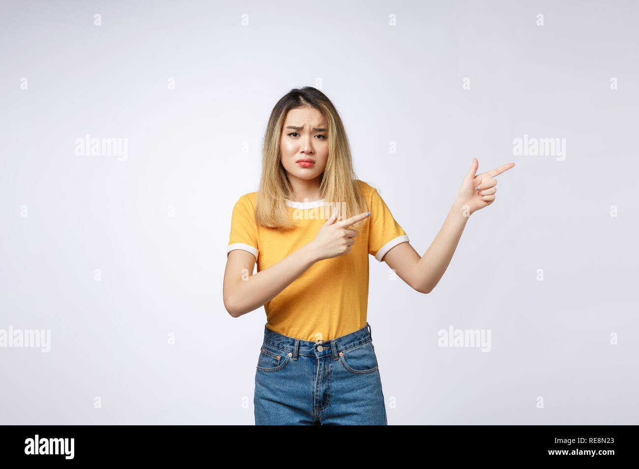 Young Asian woman looking angry and sad while pointing finger at camera ...