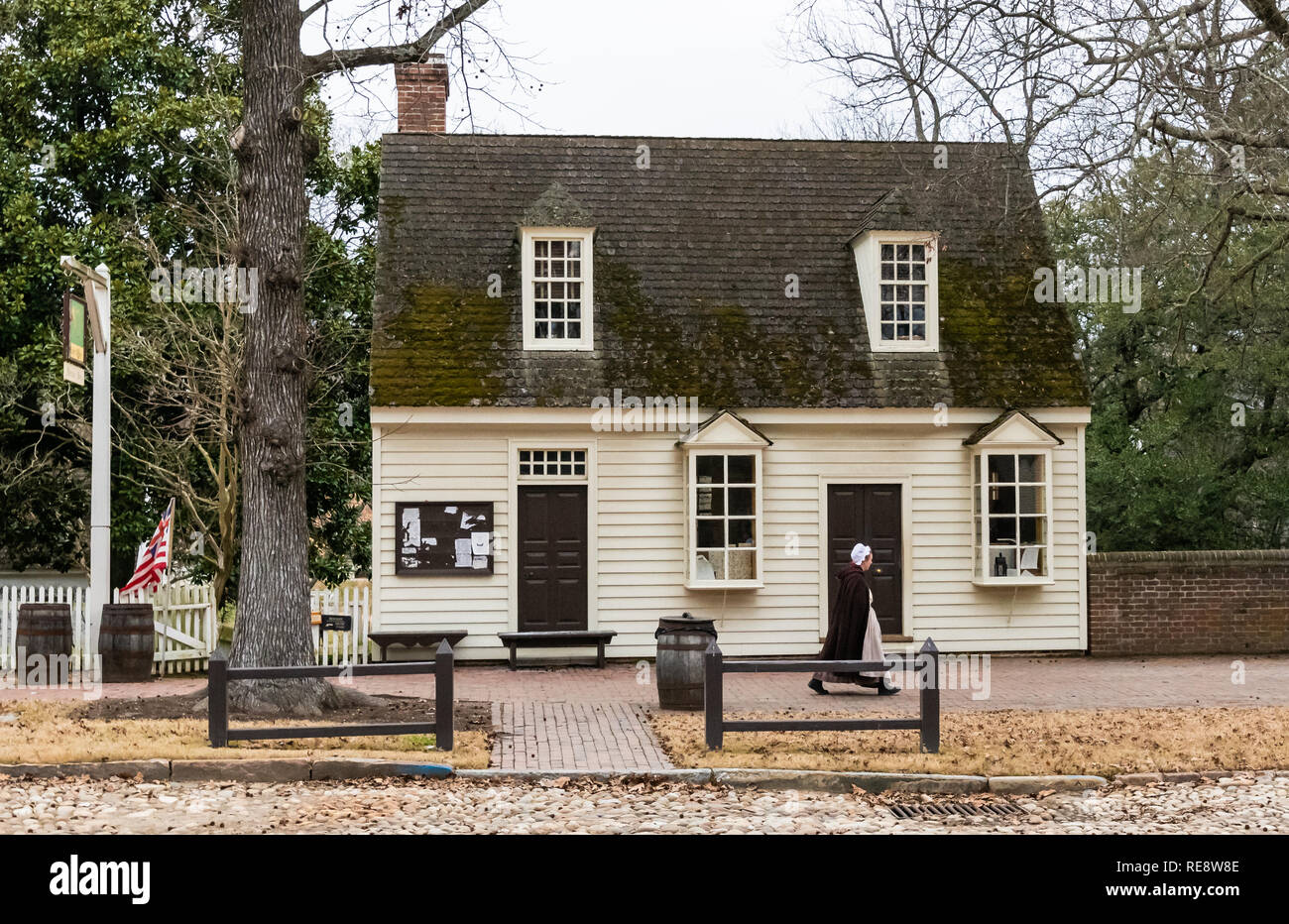 A colonial reenactor woman walks in front of a colonial era house in ...