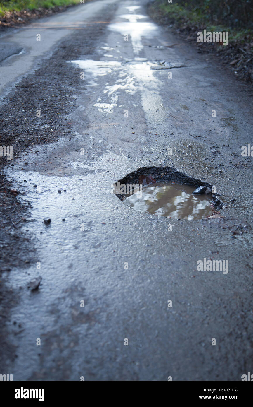 Pothole in country road in English countryside. Asphalt road needing ...