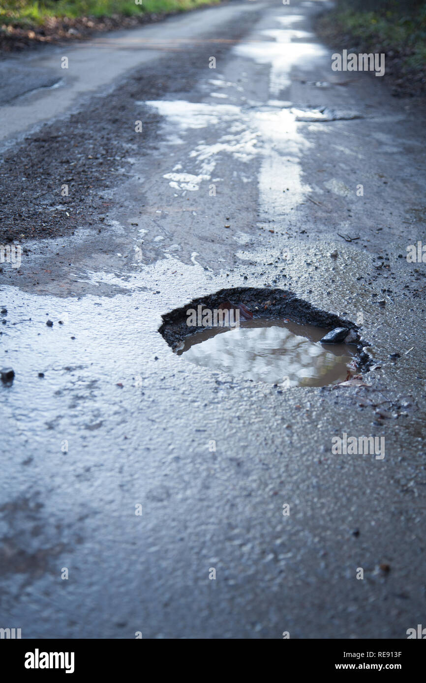 Pothole in country road in English countryside. Asphalt road needing ...