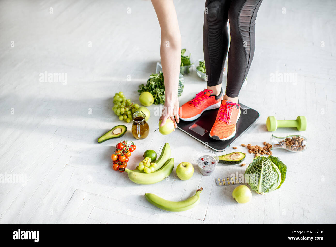Sports woman weighing on the scales with healthy food around. Weight ...