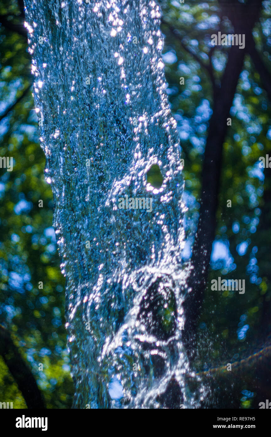 transparent falling water vertical flows against a blue sky and green ...