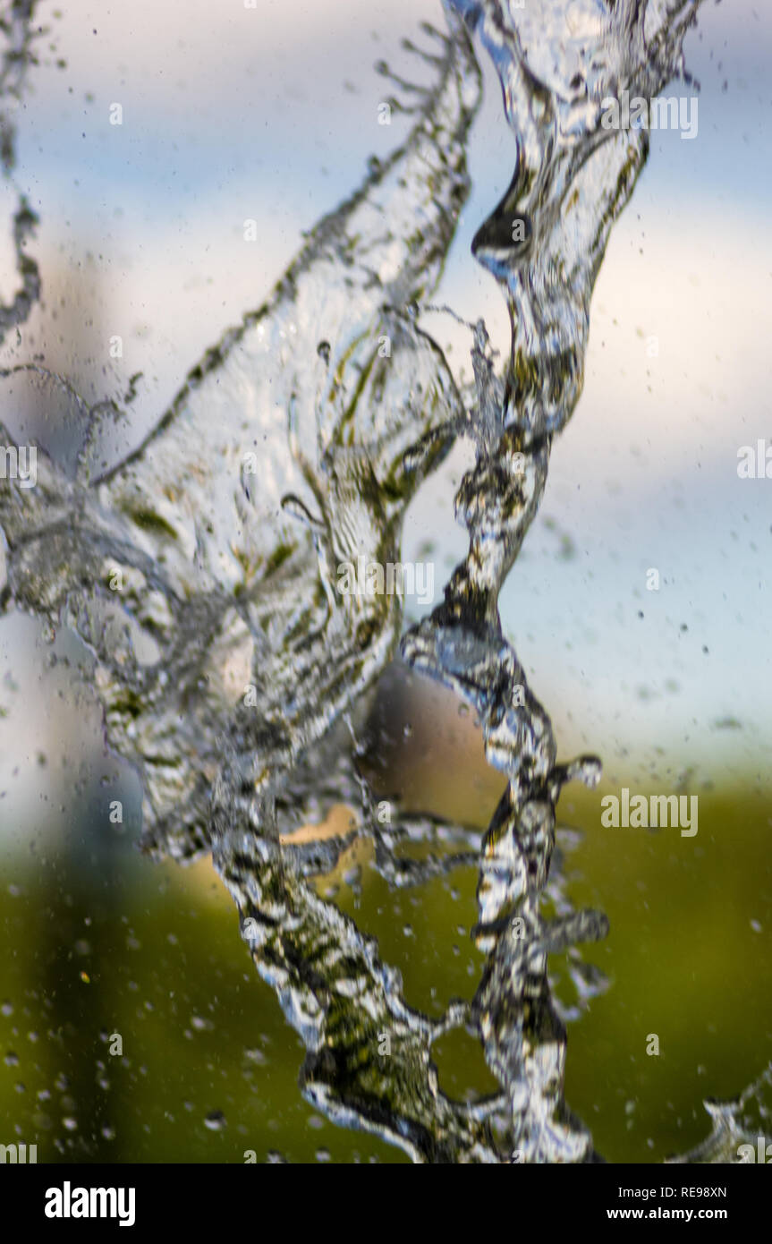transparent falling water vertical flows against a blue sky and green ...