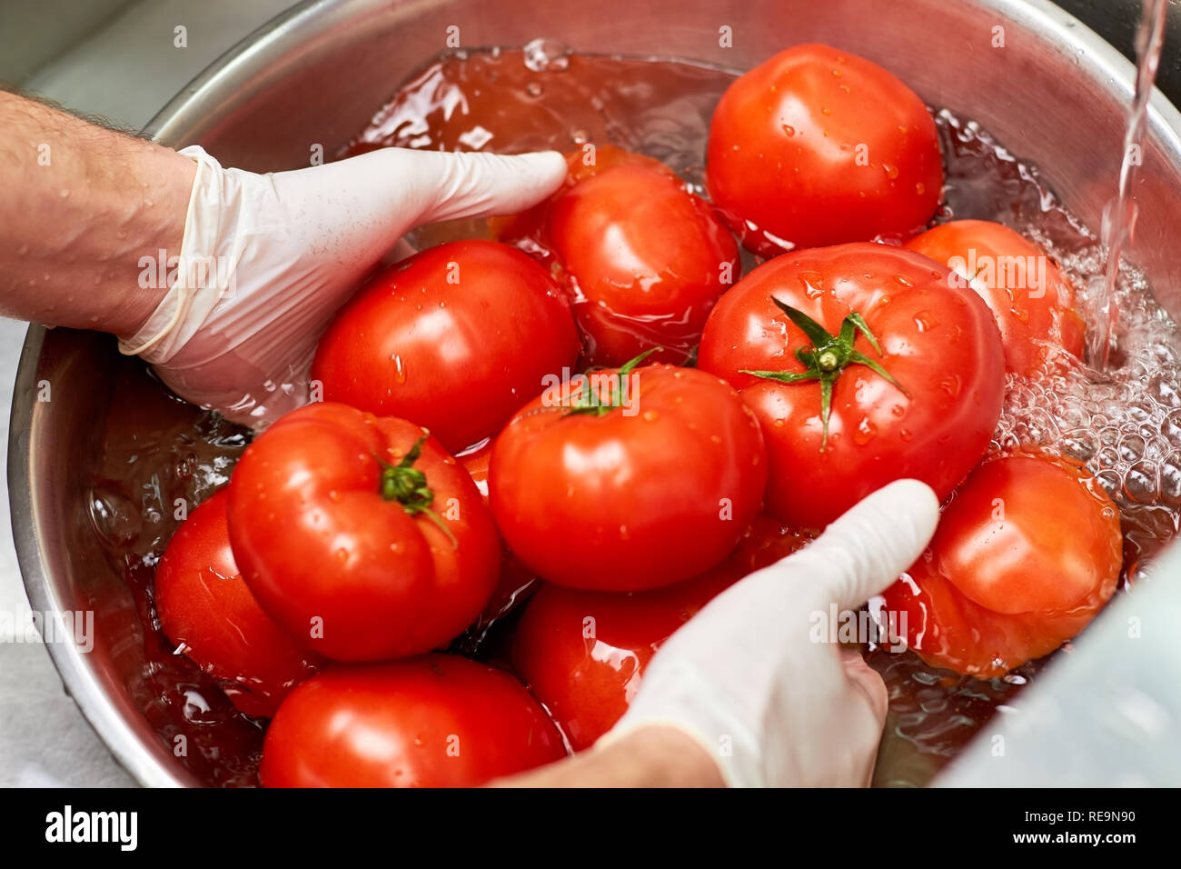 Rinsing tomatoes in water in metal bowl. Chef hands washing pile of ...