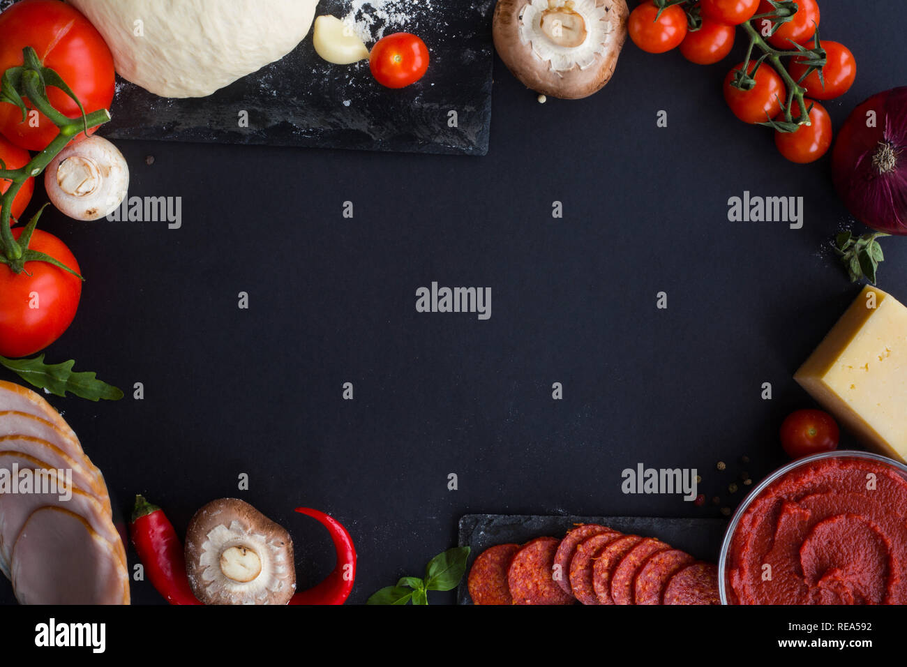 Raw dough for pizza with ingredients and spices on black table ...