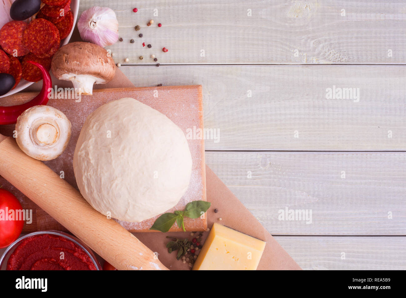 Raw dough for pizza with ingredients and spices on white wooden table ...