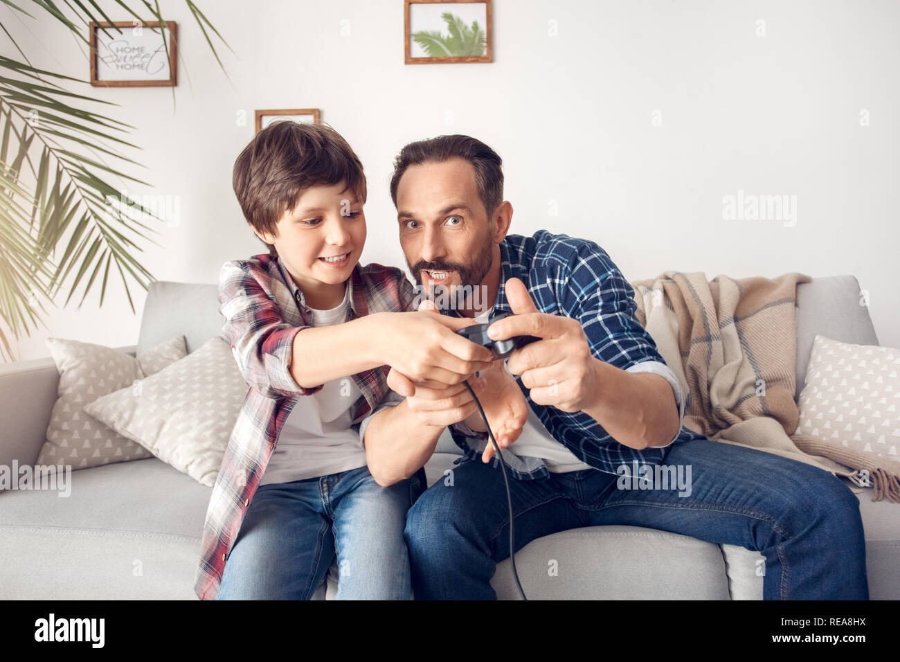 Father and little son at home sitting on sofa holding controller ...