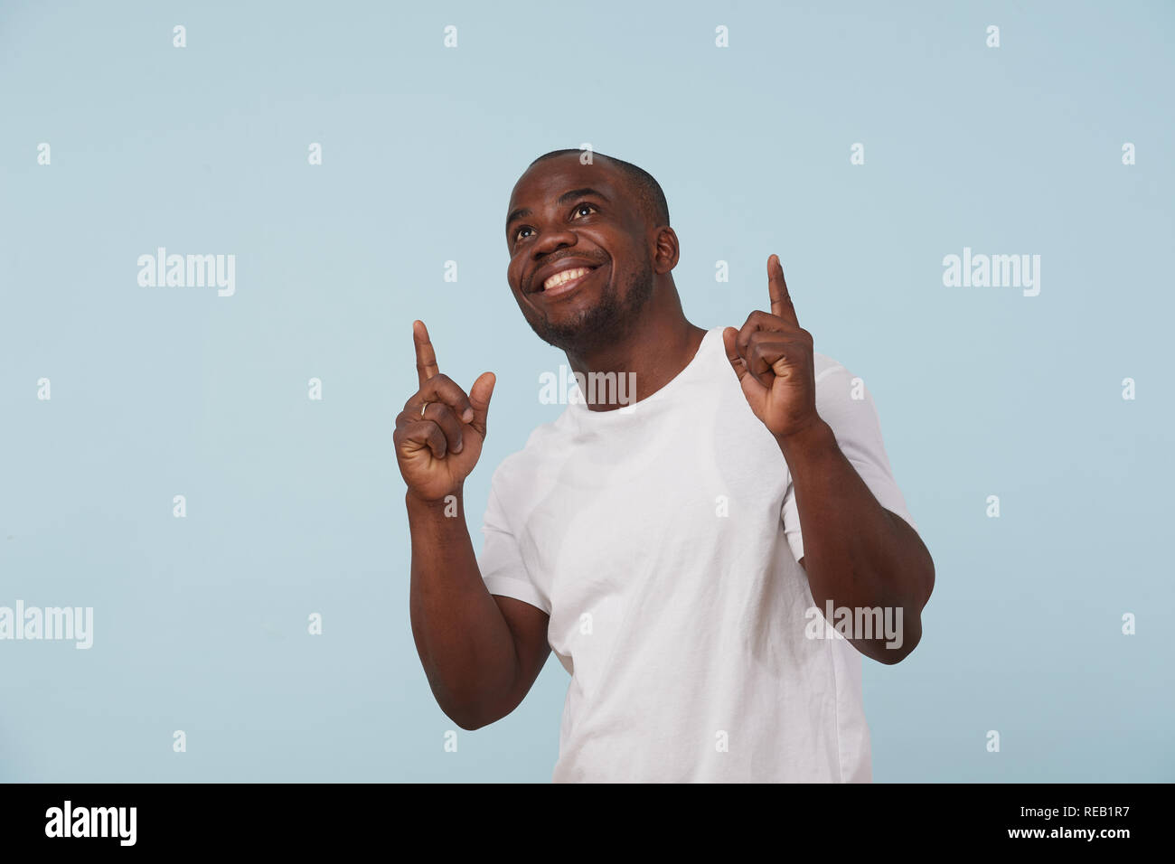 Handsome bold black man in white T-shirt grimacing against pale blue ...