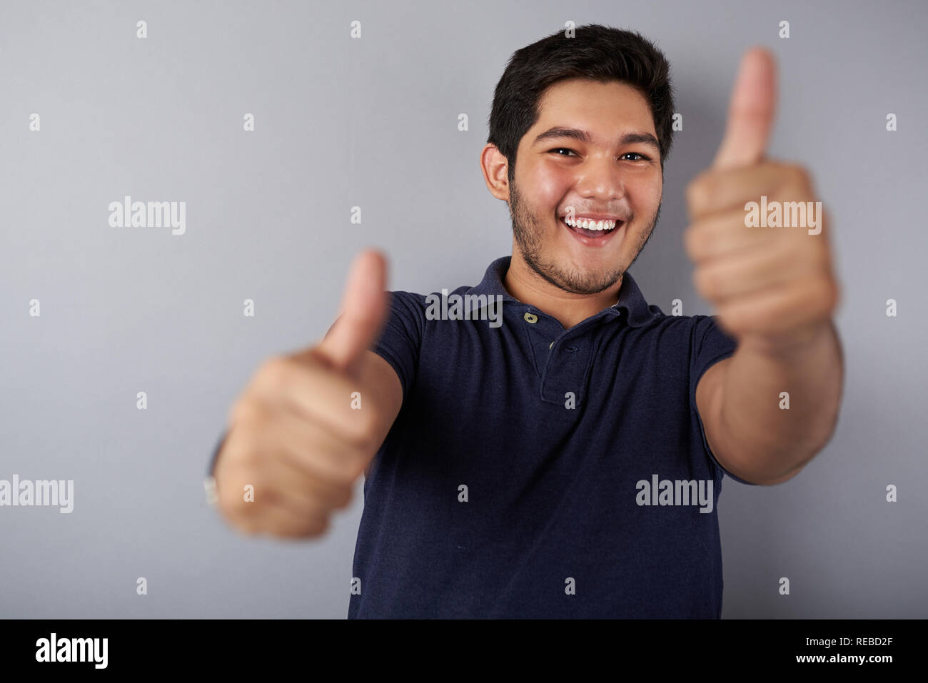 Happy smiling young man showing thumb up isolated on gray background ...
