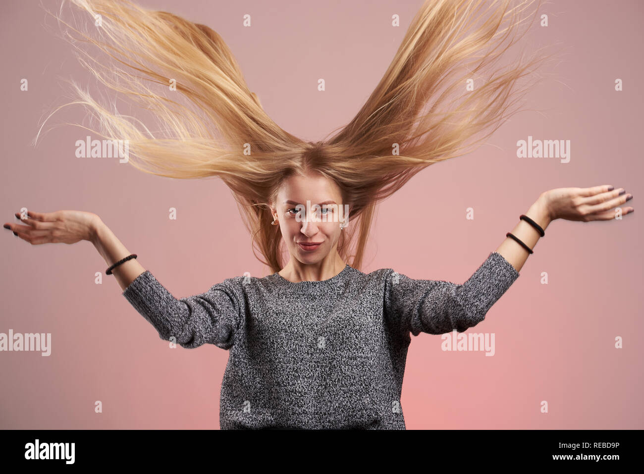 Young blonde girl with long hair flying around isolated on pink ...