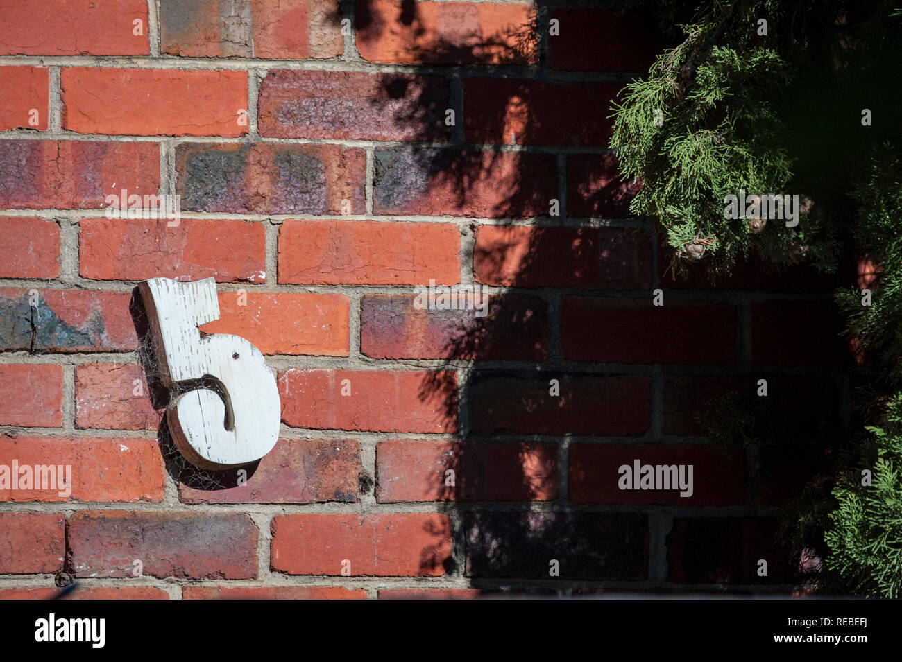 A broken wooden number 5 on a brick wall in the sunshine with shadow of ...
