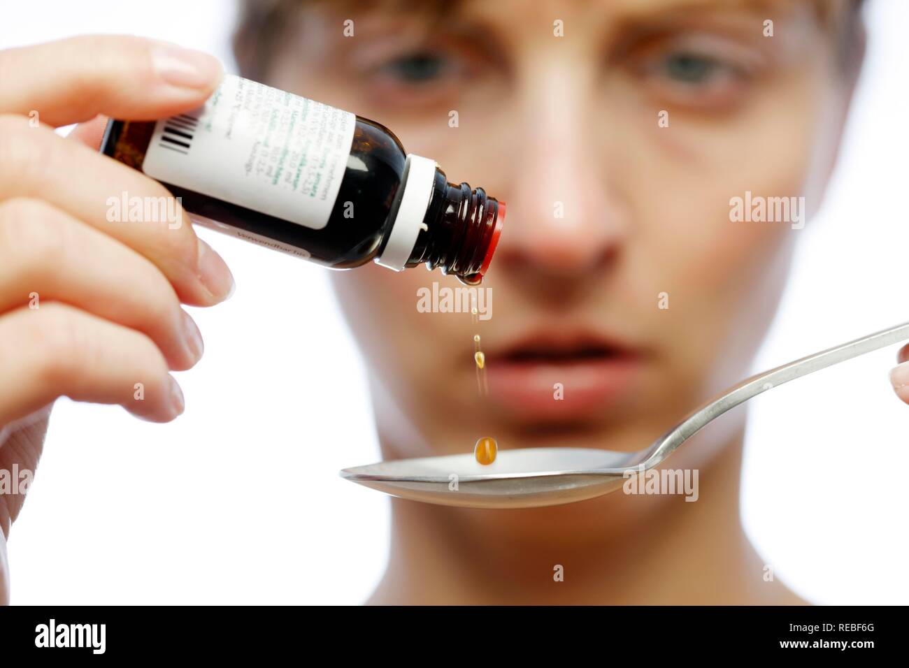 Young woman dripping liquid medicine onto a spoon, against a cold or ...