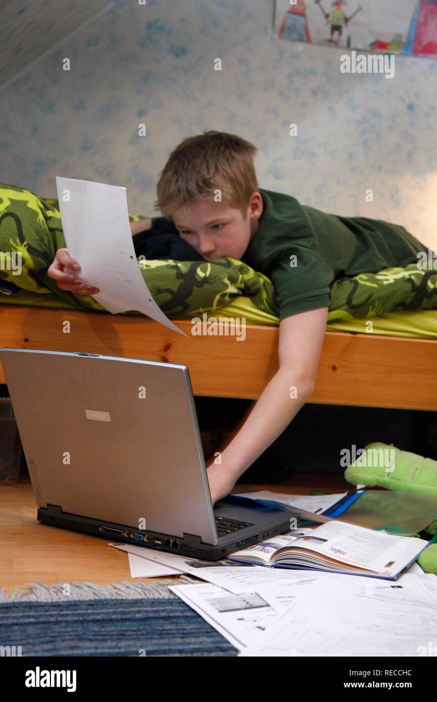 Boy, 11 years old, working with his computer at home in his room, doing ...