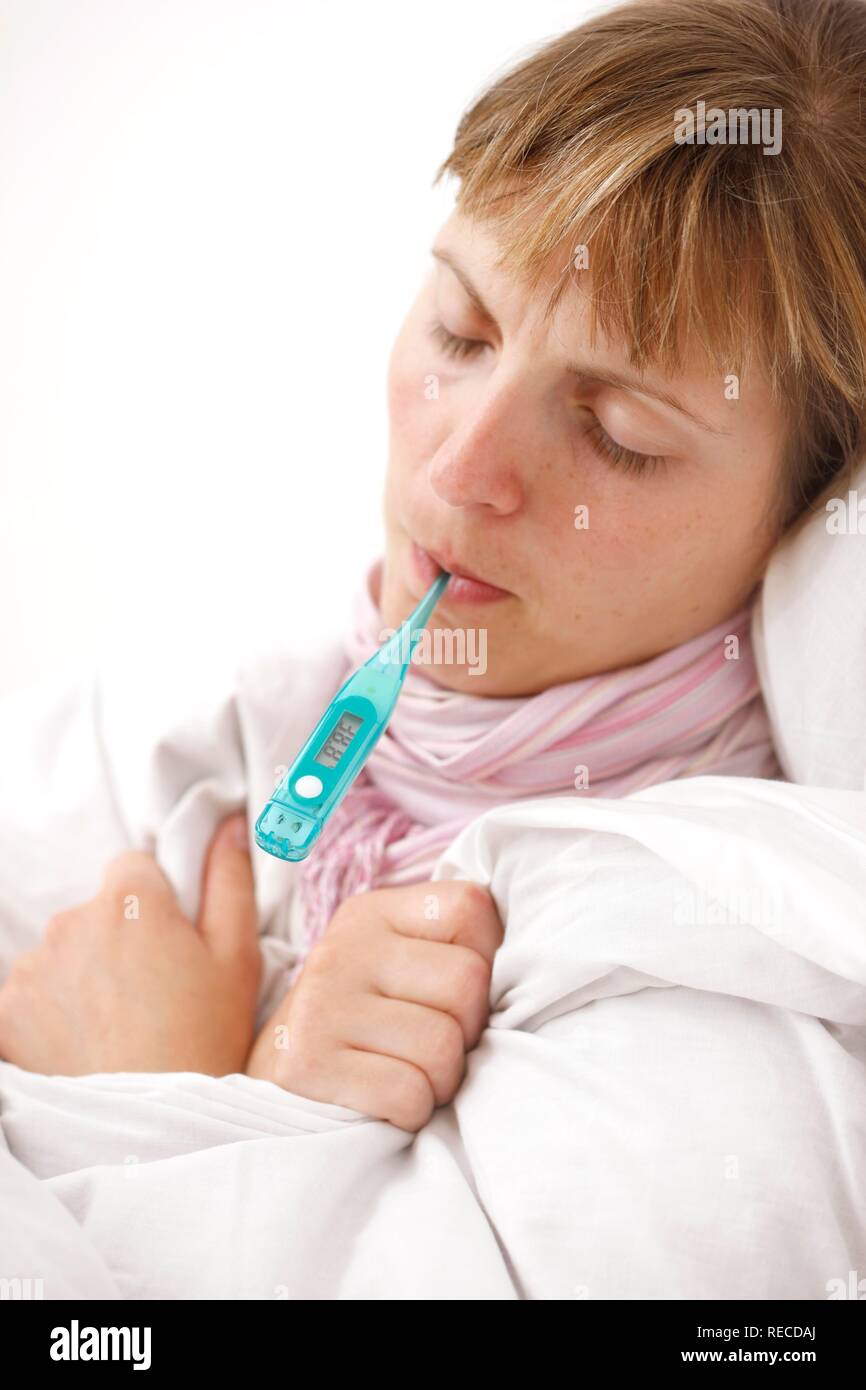 Young woman, sick in bed with fever, measuring her body temperature ...