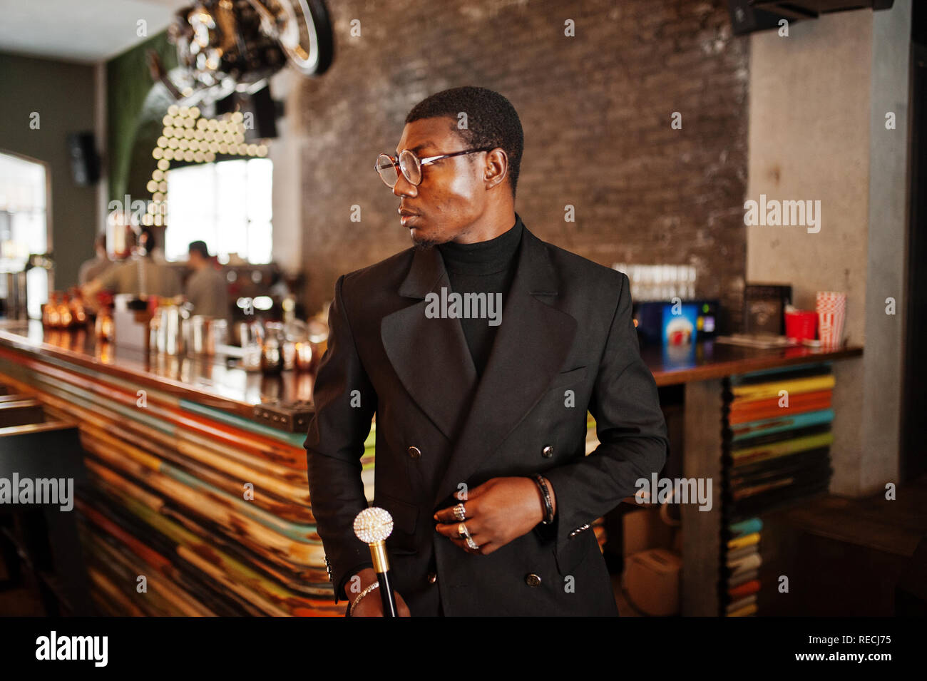 Stylish african american gentleman in elegant black jacket and glasses, holding retro walking ...
