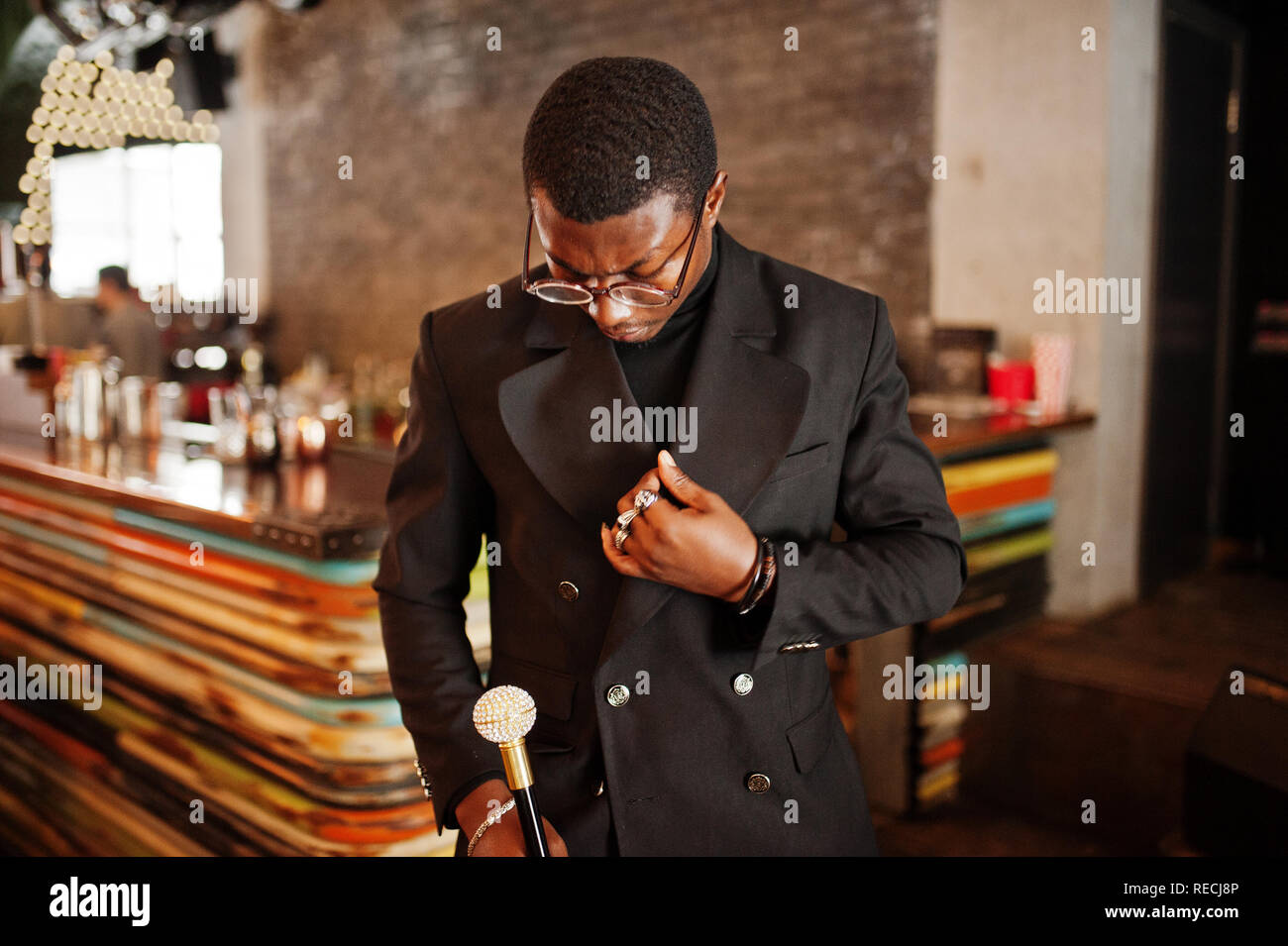 Stylish african american gentleman in elegant black jacket and glasses, holding retro walking ...