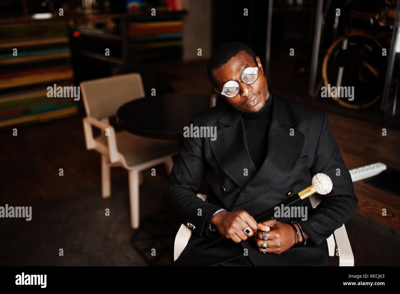 Stylish african american gentleman in elegant black jacket and glasses, holding retro walking ...