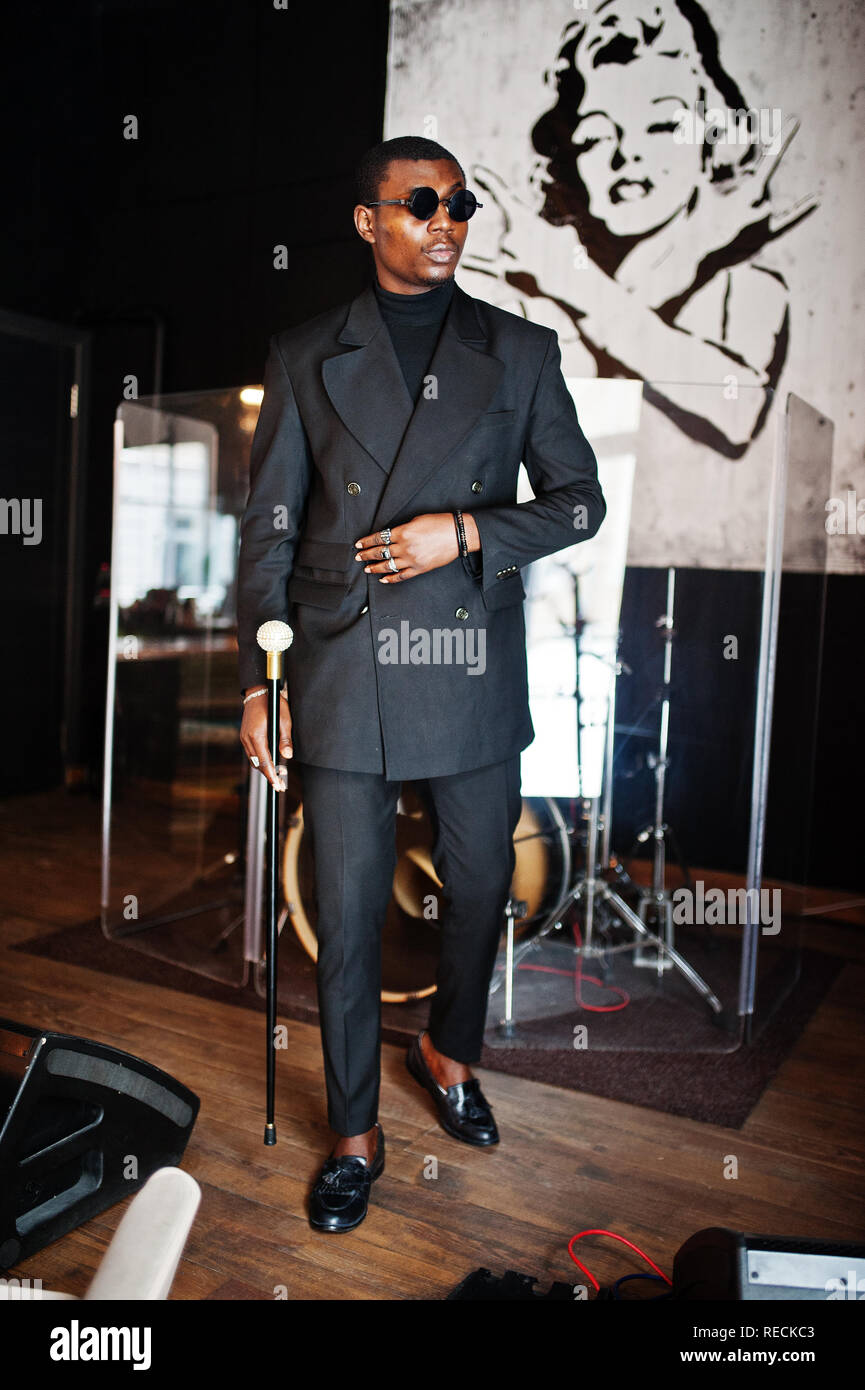 Stylish african american gentleman in elegant black jacket and sunglasses, holding retro walking ...
