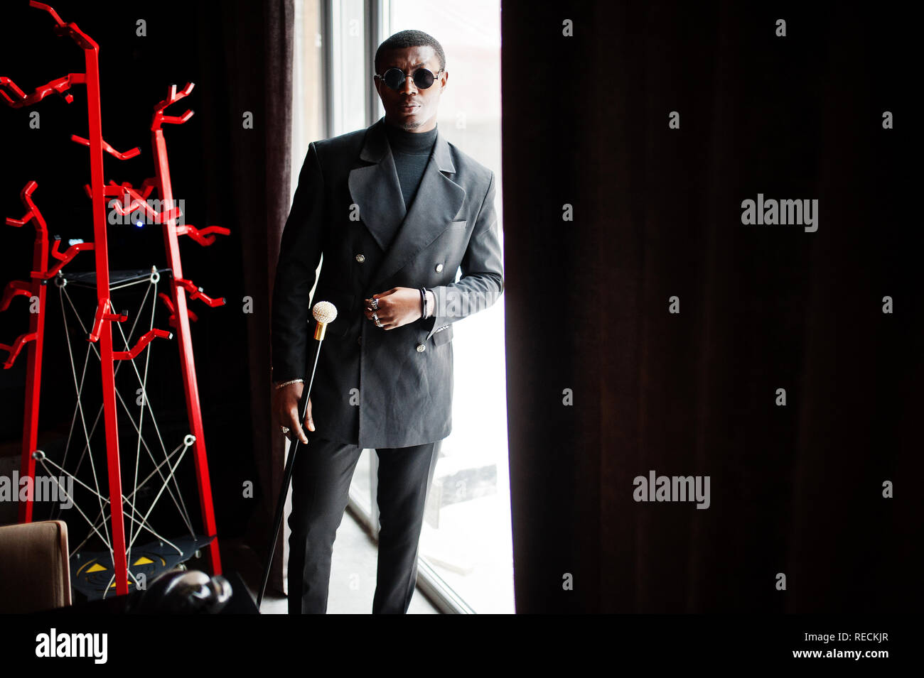 Stylish african american gentleman in elegant black jacket and sunglasses, holding retro walking ...