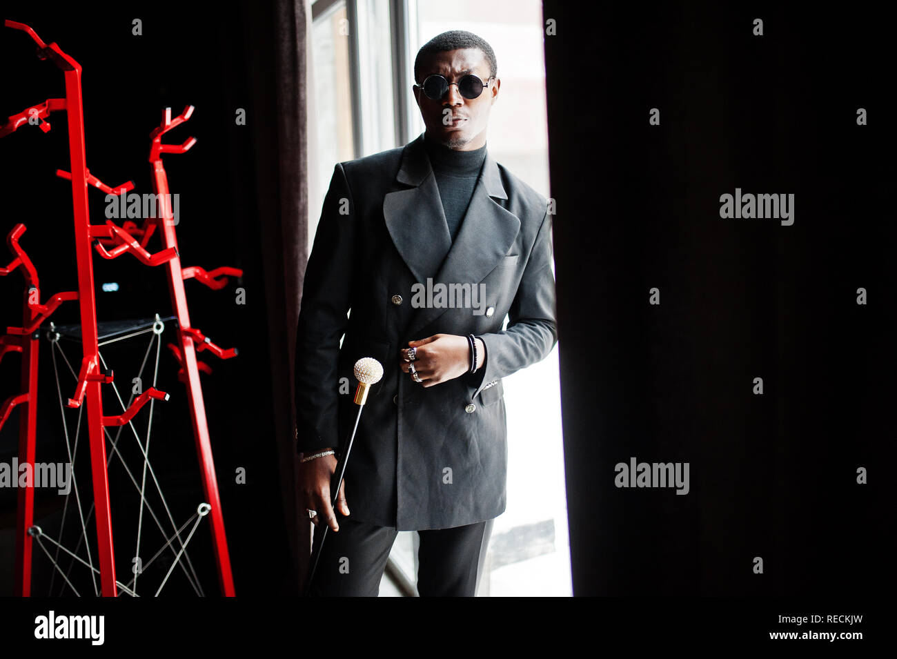 Stylish african american gentleman in elegant black jacket and sunglasses, holding retro walking ...
