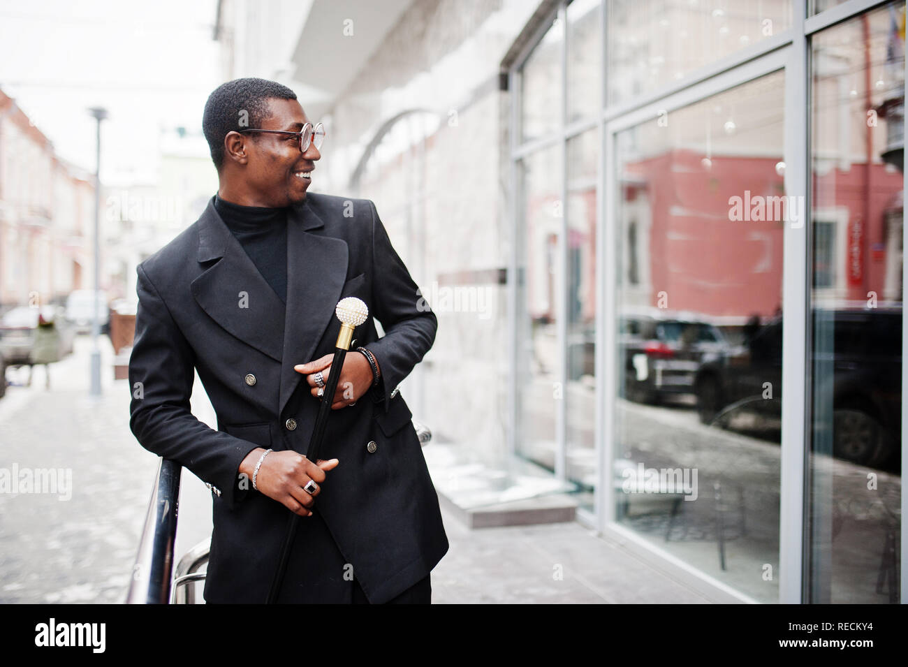 Stylish african american gentleman in elegant black jacket, holding retro walking stick as cane ...