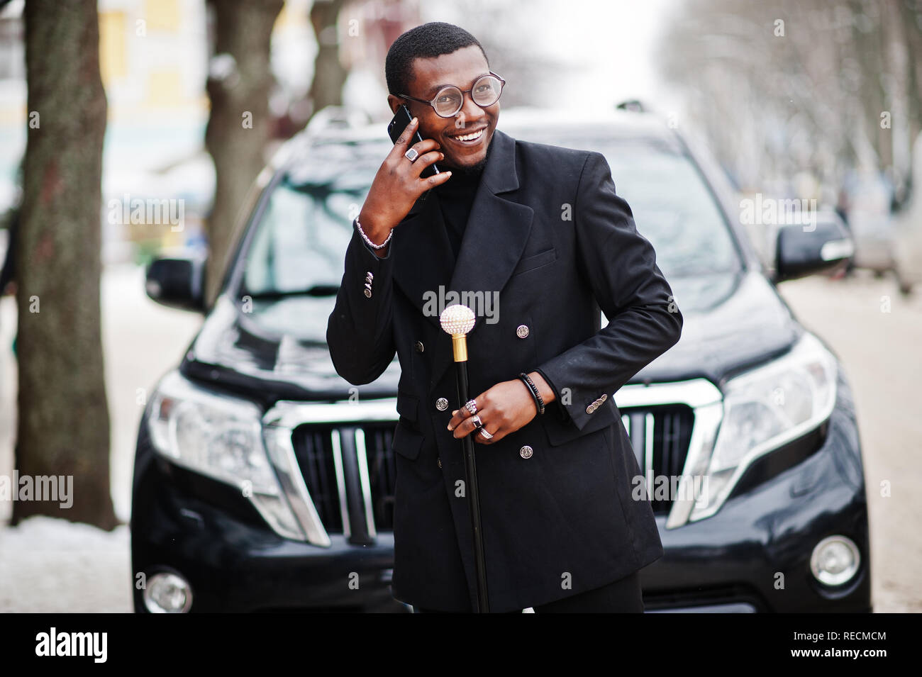 Stylish african american gentleman in elegant black jacket, holding retro walking stick as cane ...