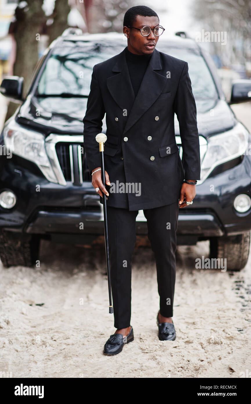 Stylish african american gentleman in elegant black jacket, holding retro walking stick as cane ...