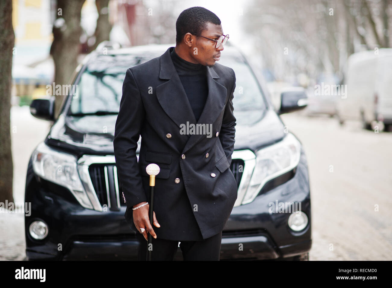 Stylish african american gentleman in elegant black jacket, holding retro walking stick as cane ...