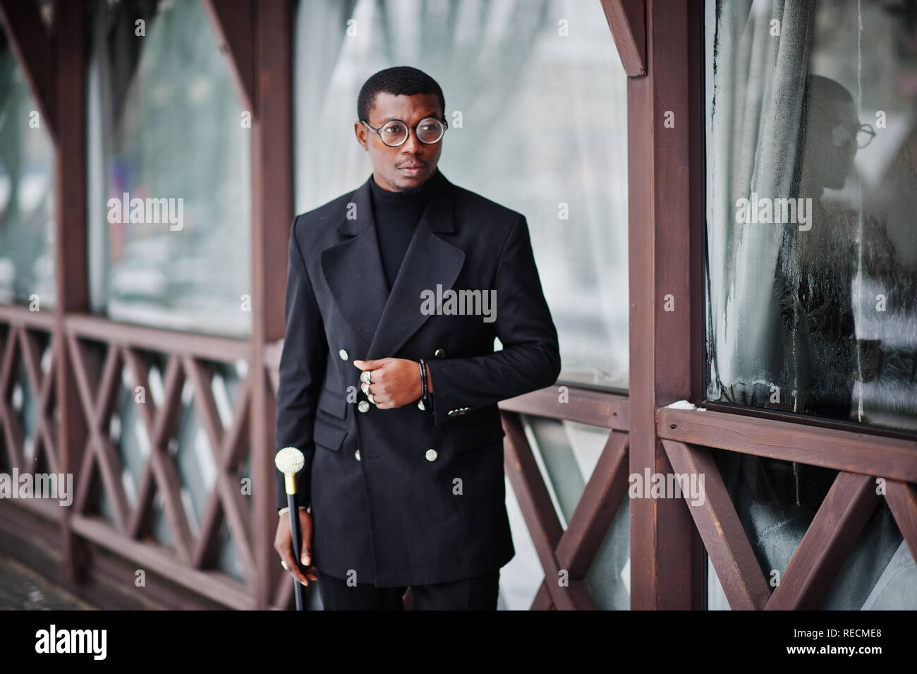 Stylish african american gentleman in elegant black jacket, holding retro walking stick as cane ...