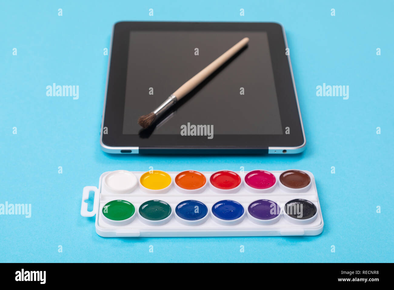 Watercolor paints and brush lying on tablet isolated on blue background ...