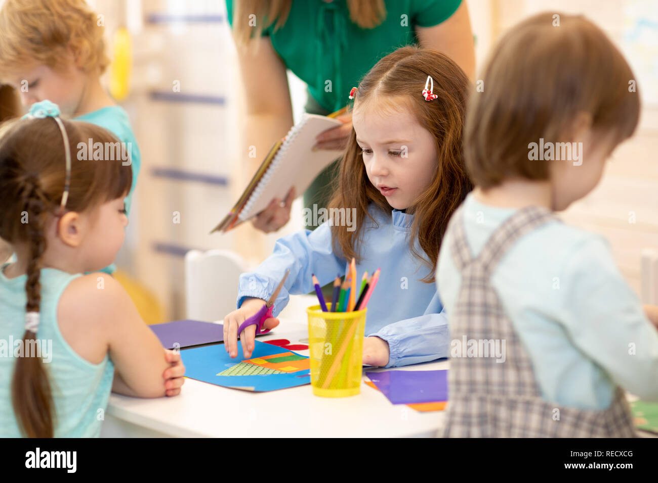 Group of preschool children working with color paper, sciccors and glue ...