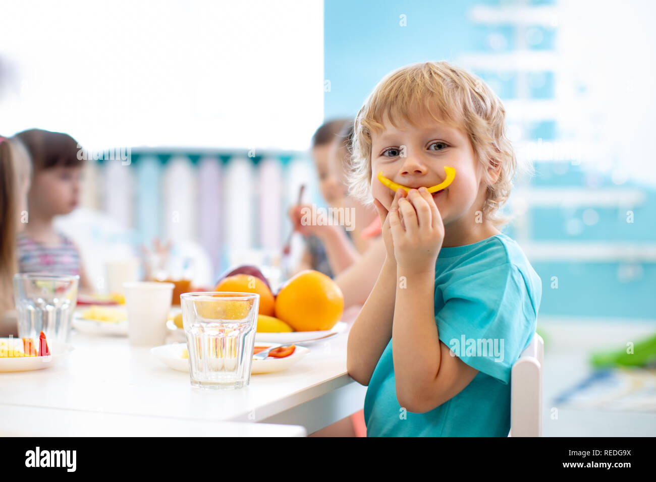 Funny kid boy eating fruits in kindergarten dining room. Child shows ...