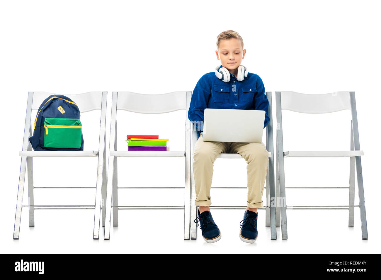 cute schoolboy sitting on chair and using laptop isolated on white ...