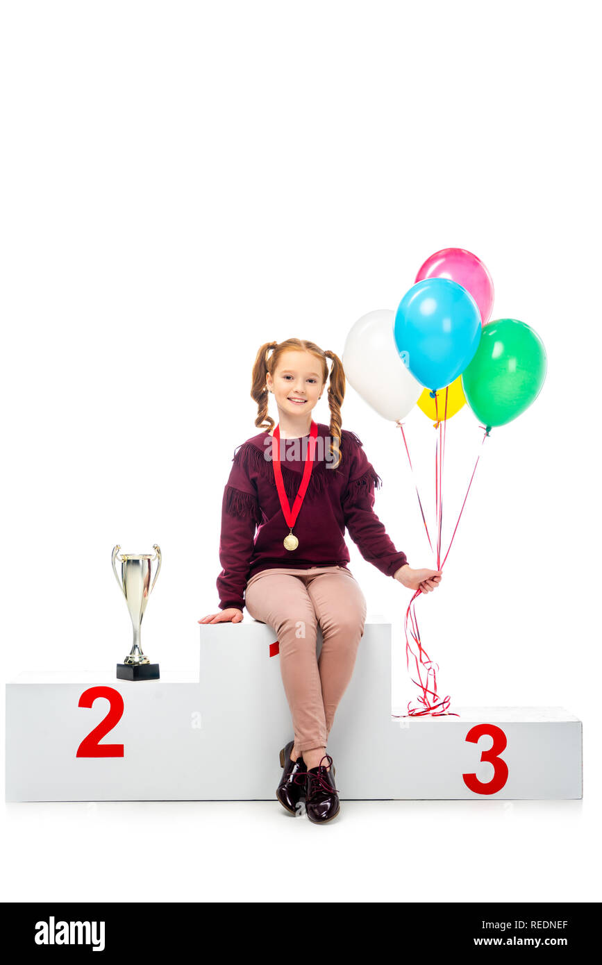 smiling schoolgirl sitting on winner podium near trophy cup, holding ...