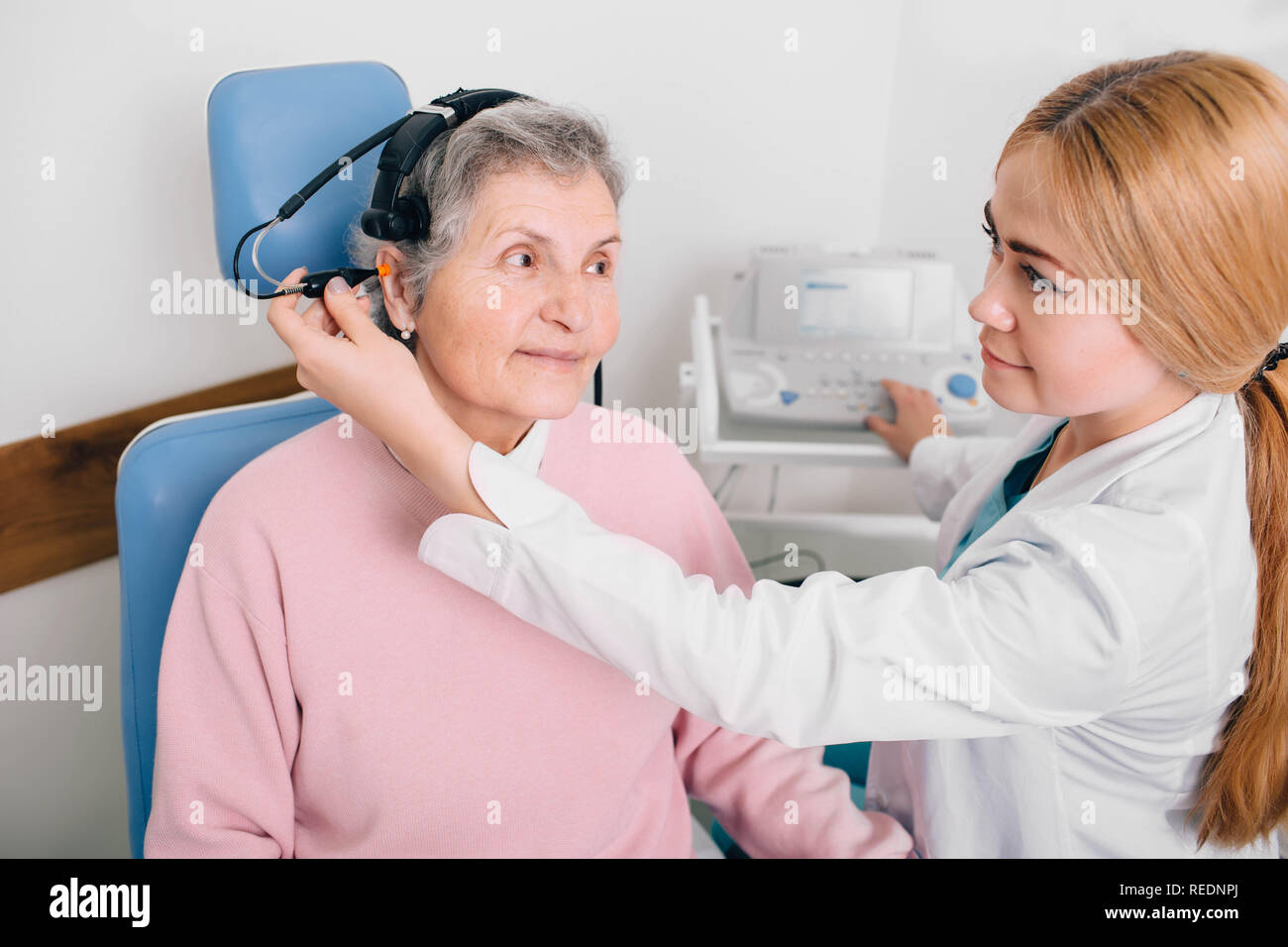 Senior patient wearing headphones, sitting near audiologist during ear ...