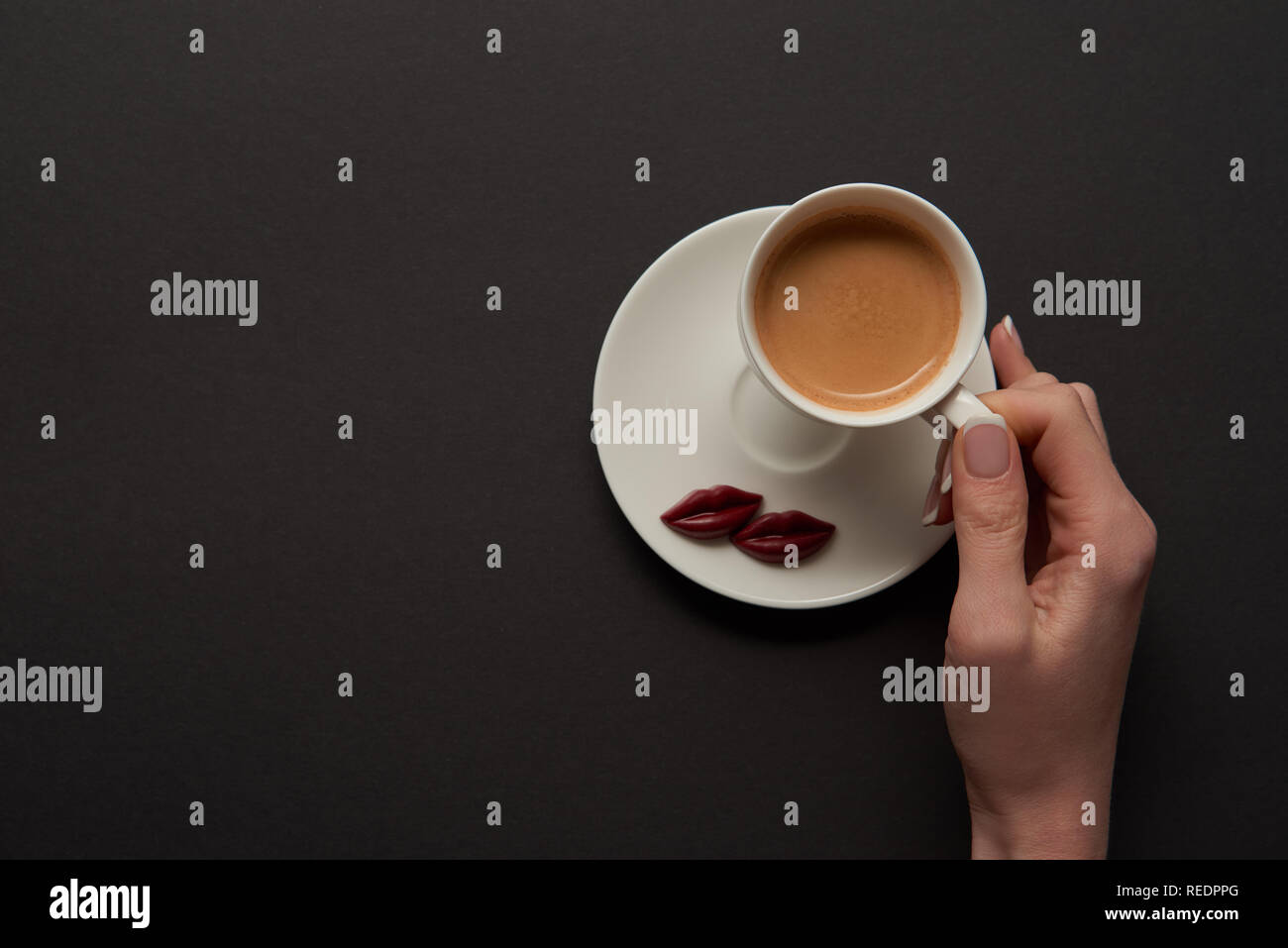 top view of woman holding cup of coffee near chocolate lips on saucer ...
