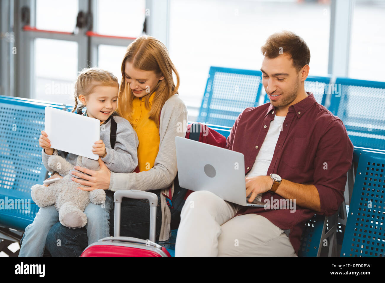 cute kid holding digital tablet near mother and looking at father using ...