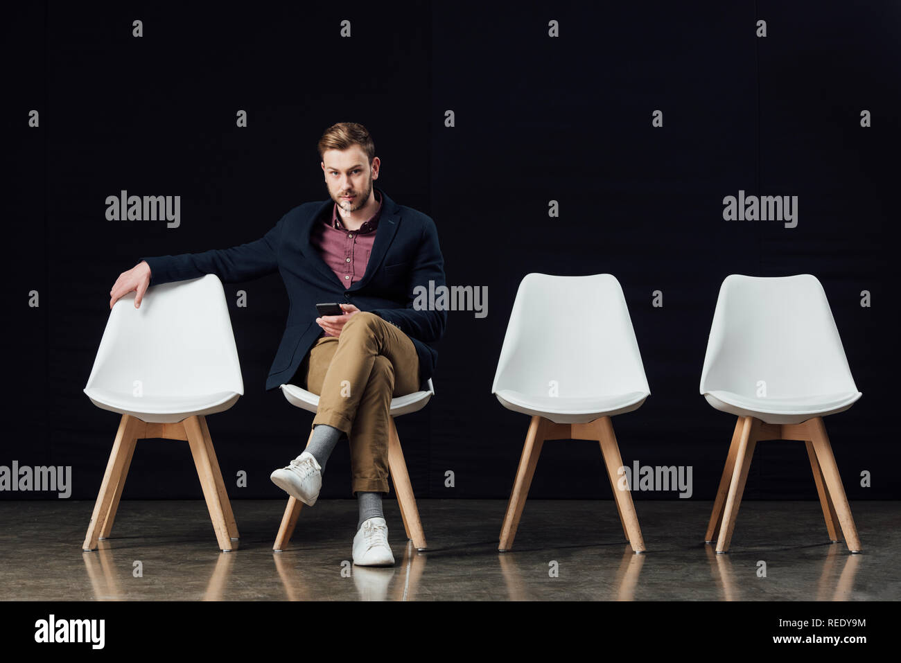 man sitting on chair, looking at camera and using smartphone isolated ...