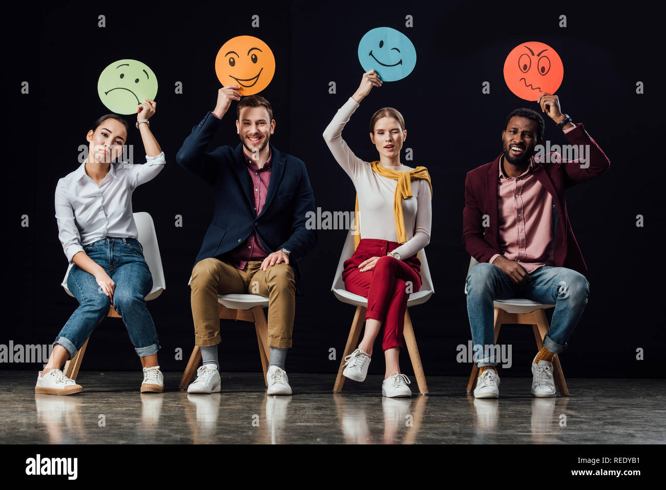 multiethnic people sitting on chairs and holding face cards with ...