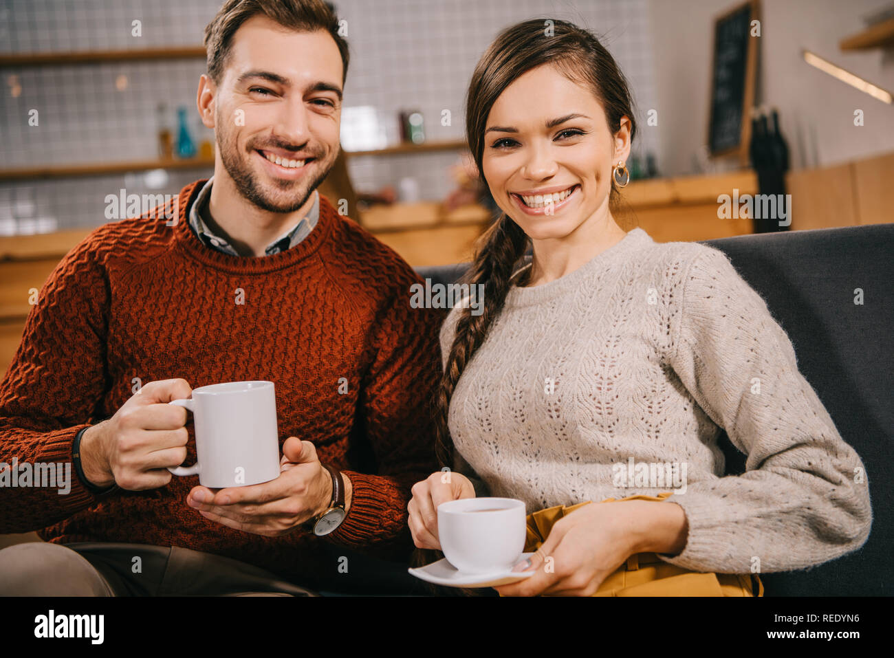 couple holding cups and smiling in cafe Stock Photo - Alamy