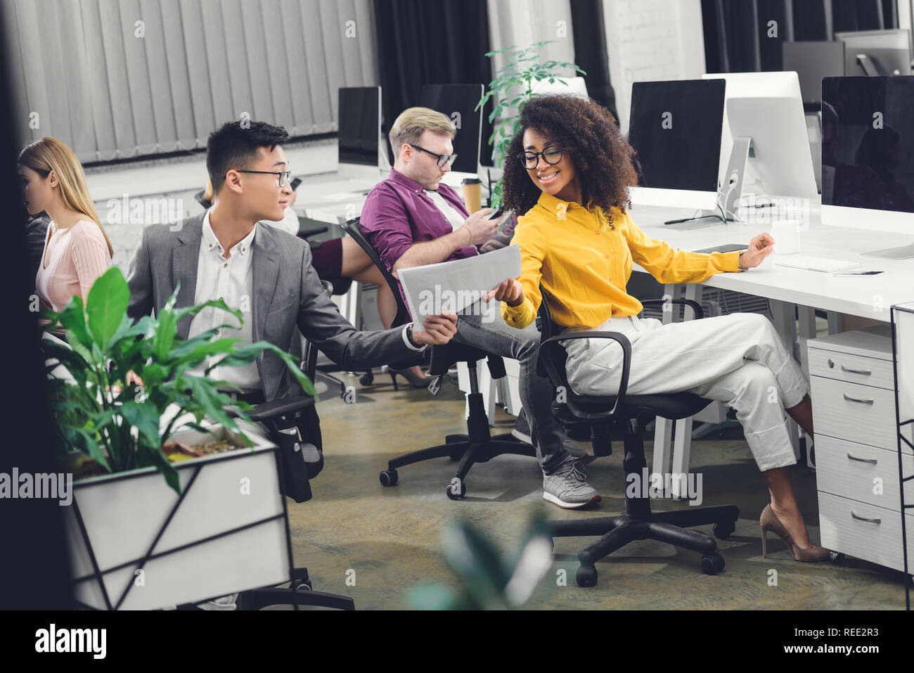 smiling young multiracial business people holding papers and working ...