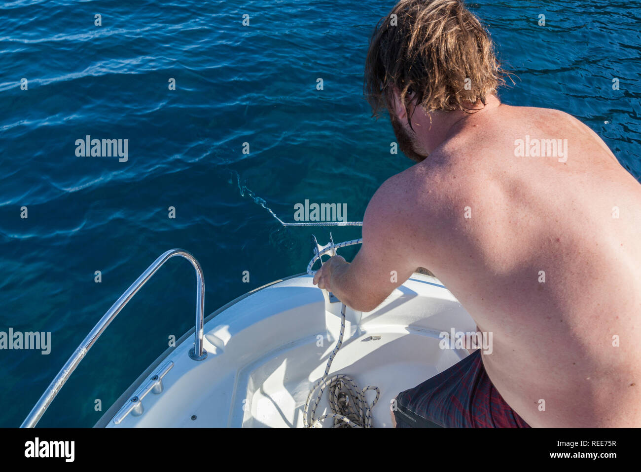 A young man on a boat pulling the rope of an anchor Stock Photo - Alamy