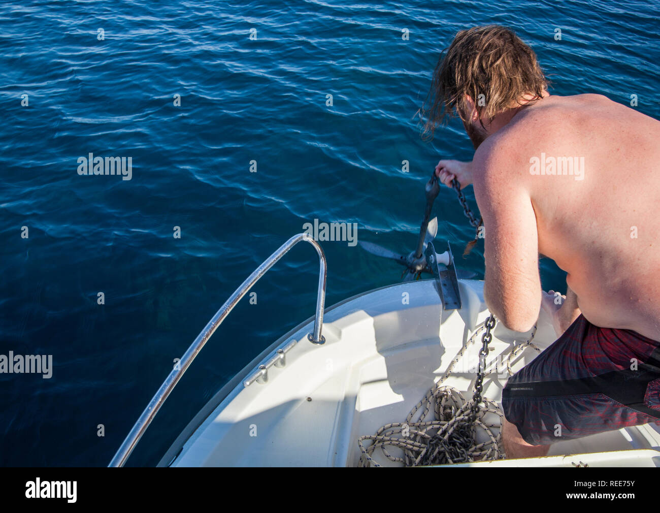 A young man on a boat pulling the rope of an anchor Stock Photo - Alamy